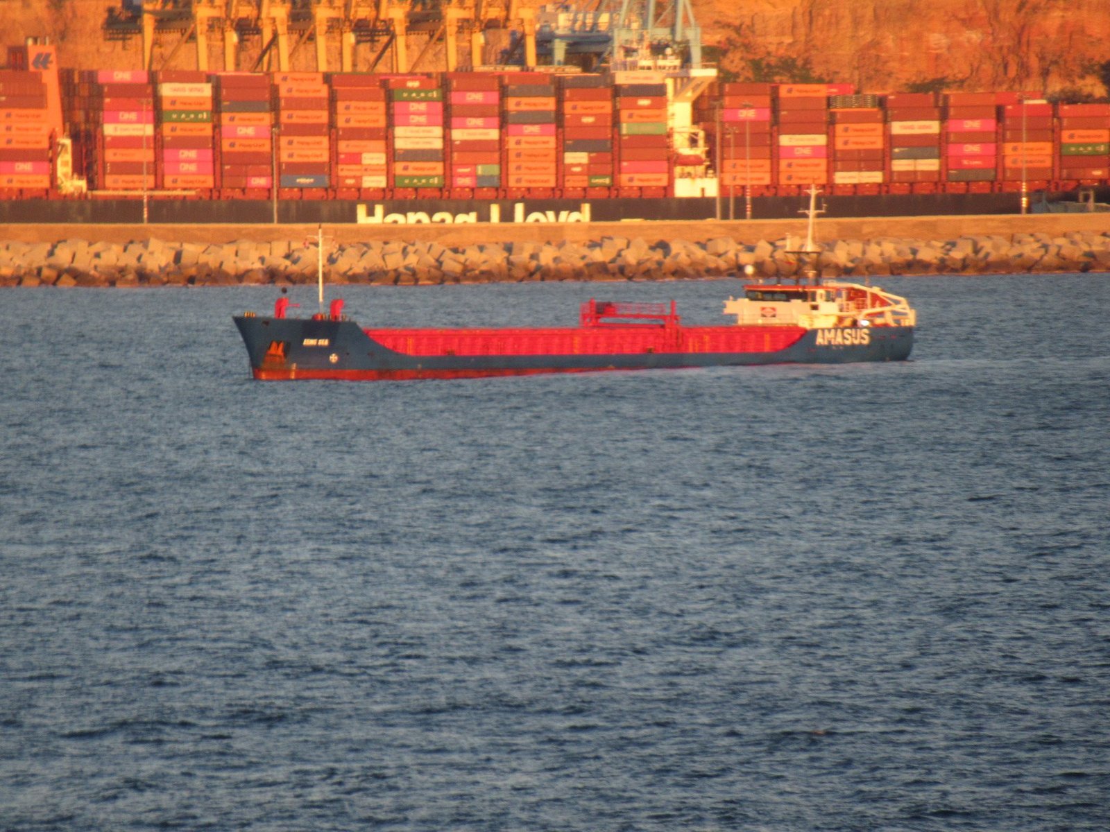 A cargo ship sailing on a calm sea, with a container port in the ...